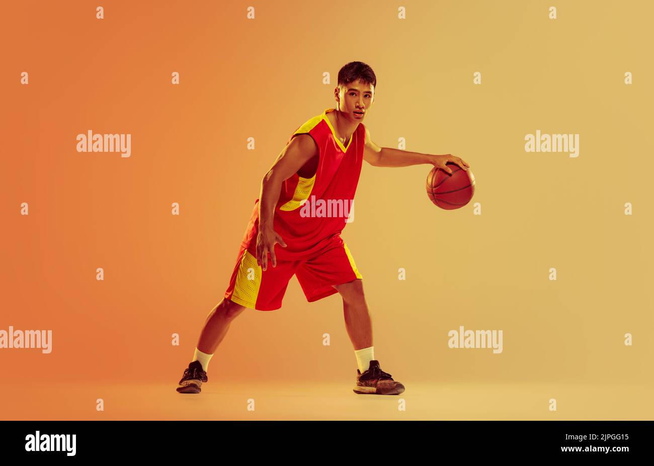 Portrait of young man, basketball player training isolated over orange ...