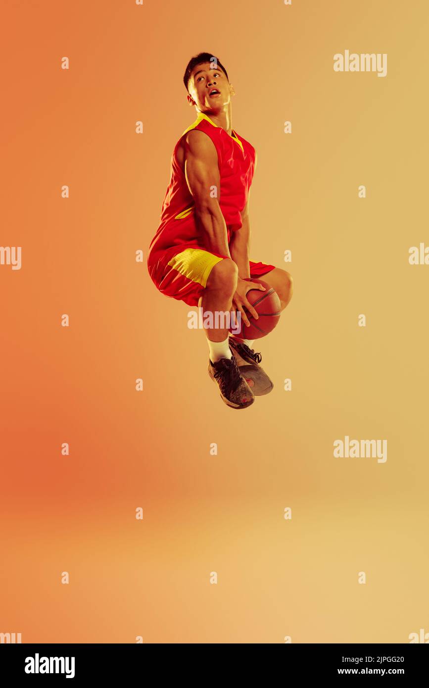 Portrait of young man, basketball player throwing ball in high jump ...