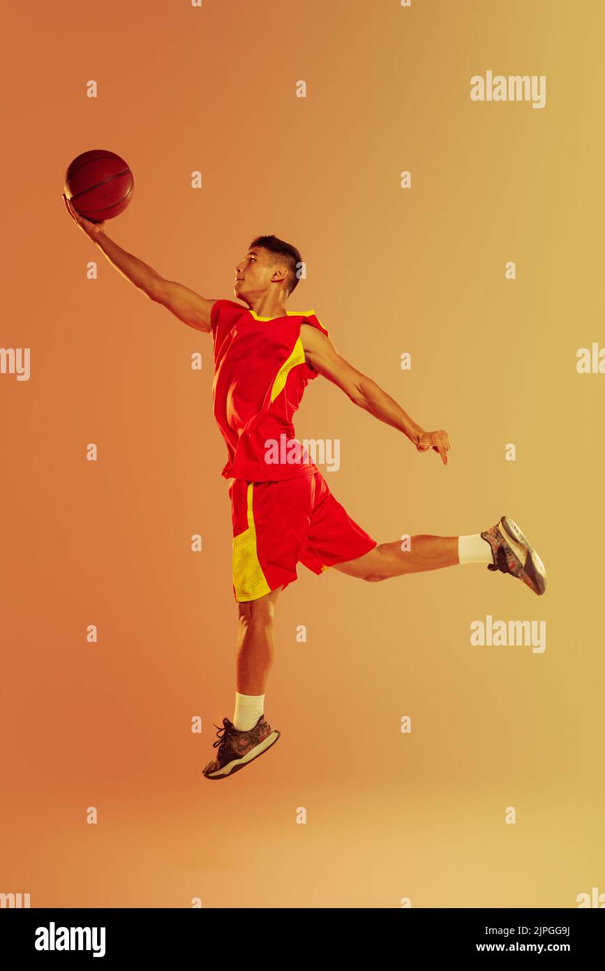Portrait of young man, basketball player isolated over orange studio ...