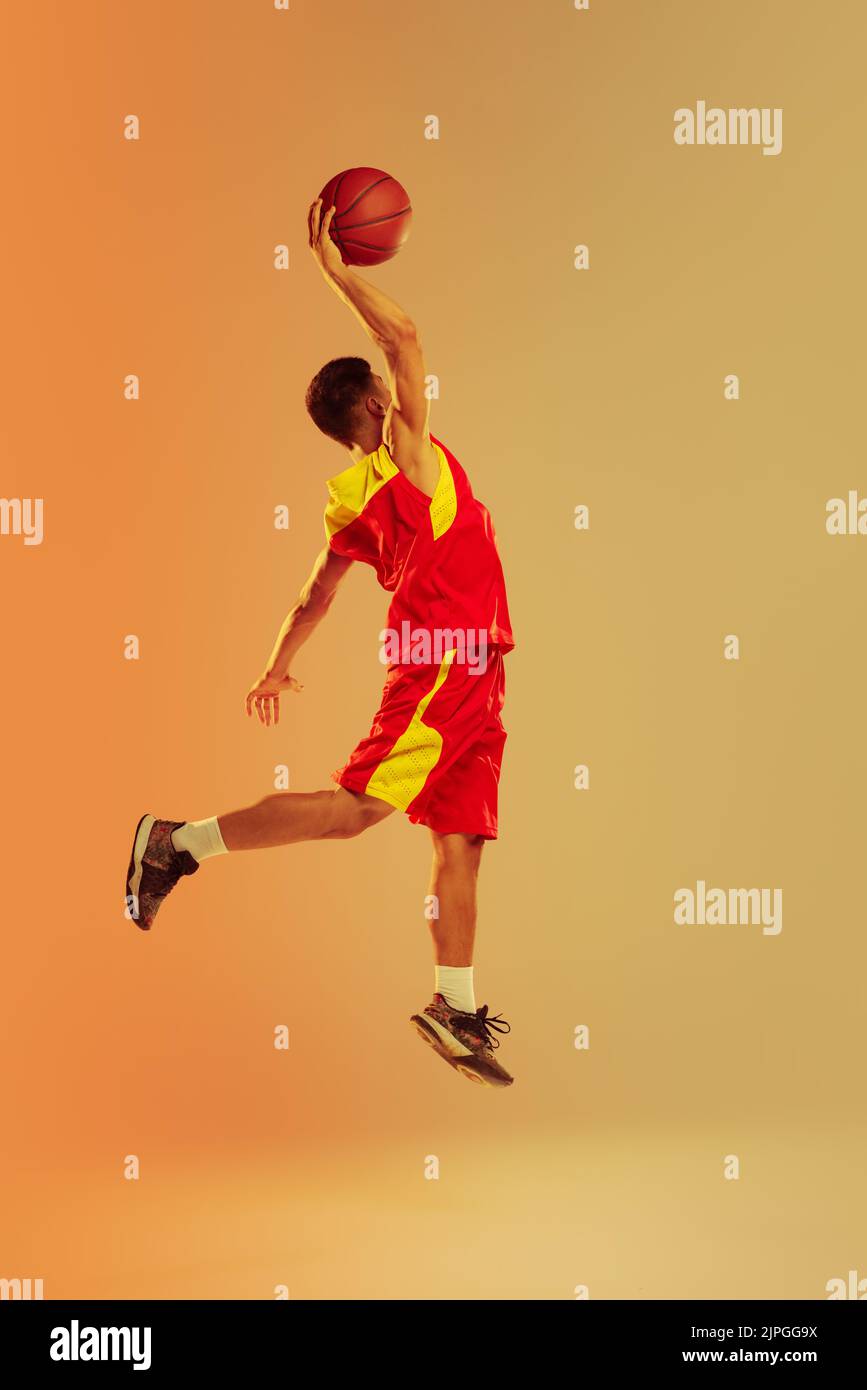 Portrait of young man, basketball player isolated over orange studio ...