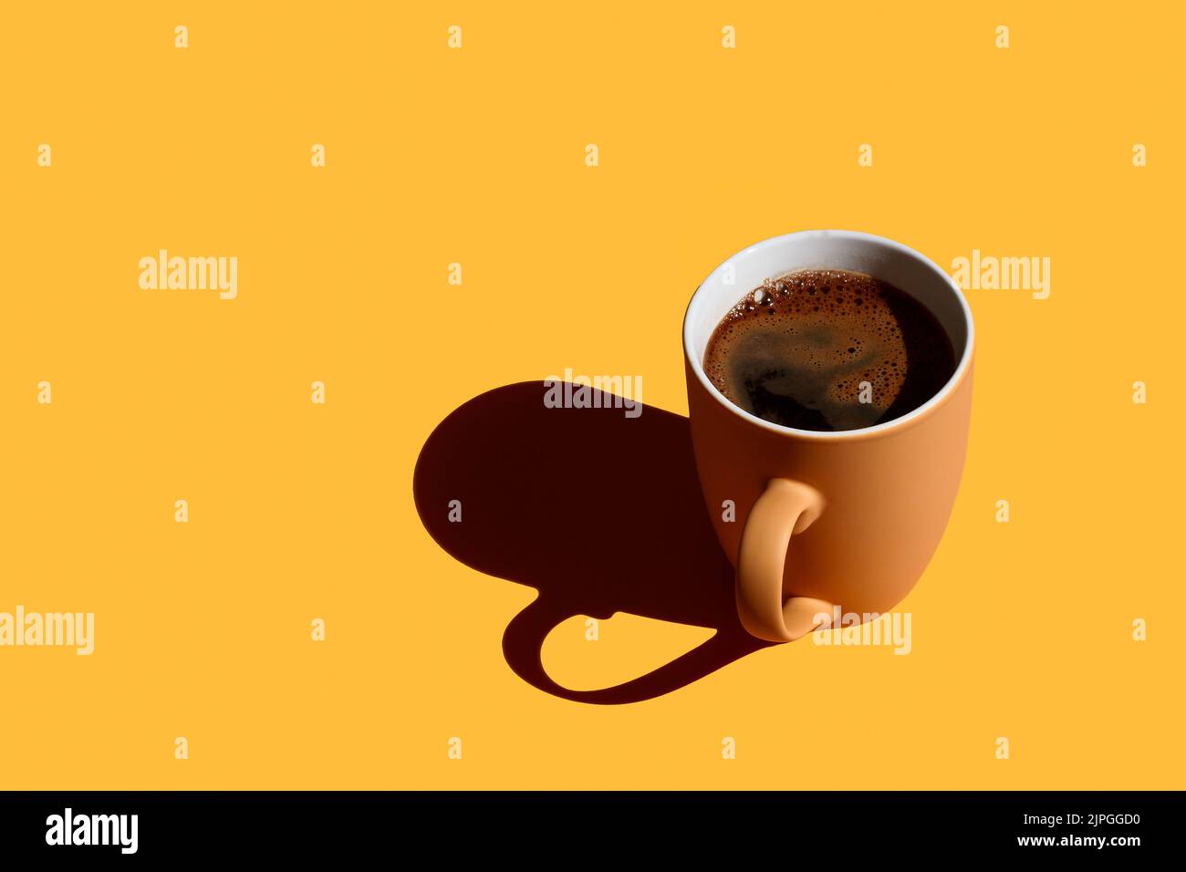 Brown mug full of coffee with hard shadow on yellow background with ...