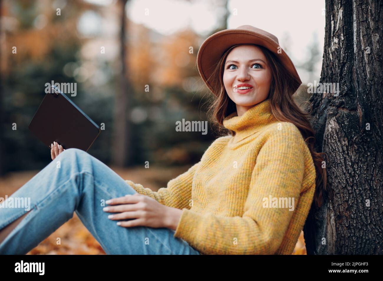 Young woman model sitting with digital tablet in autumn park with ...