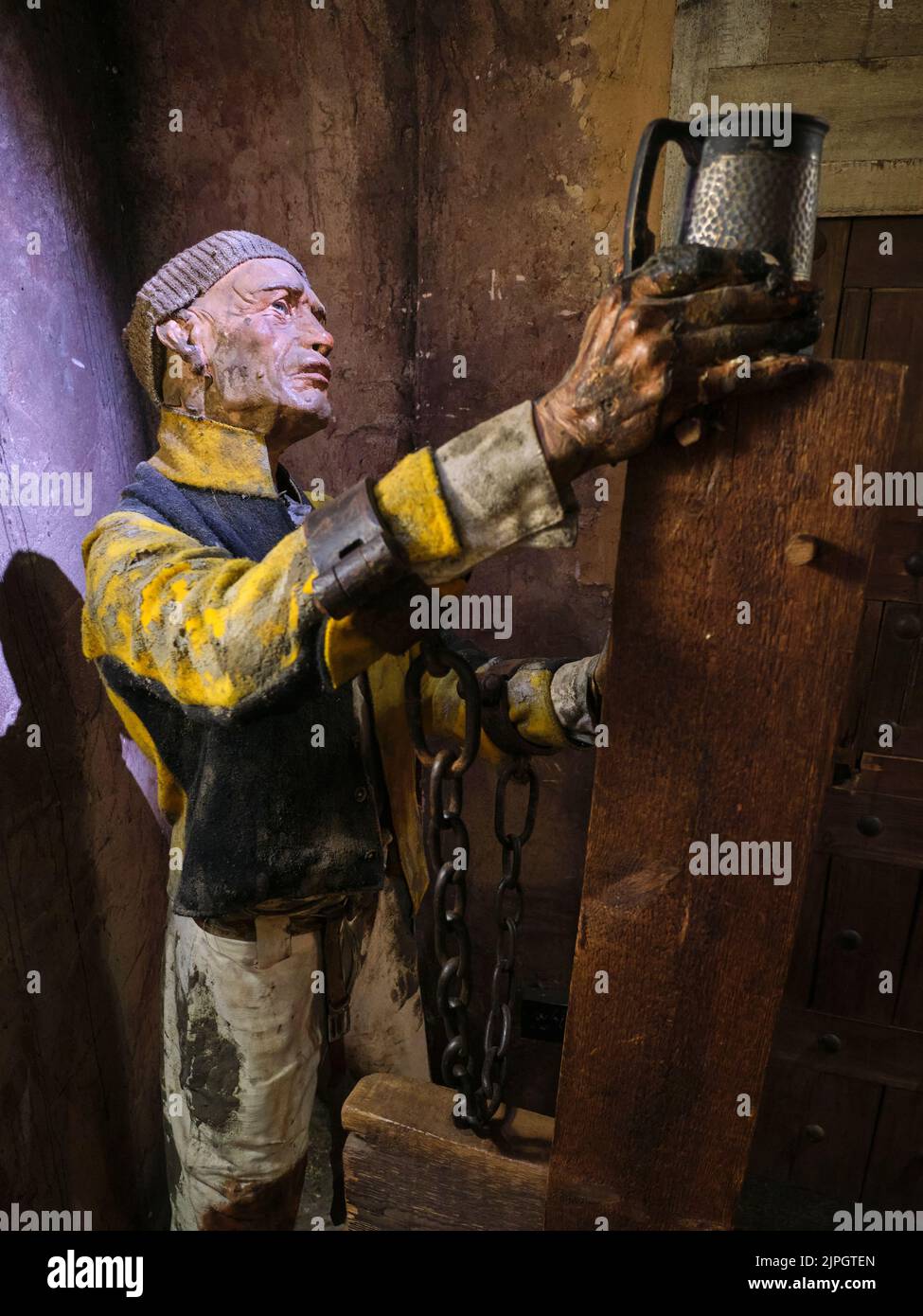 An old man prisoner, having a drink while chained to a stockade. At the ...