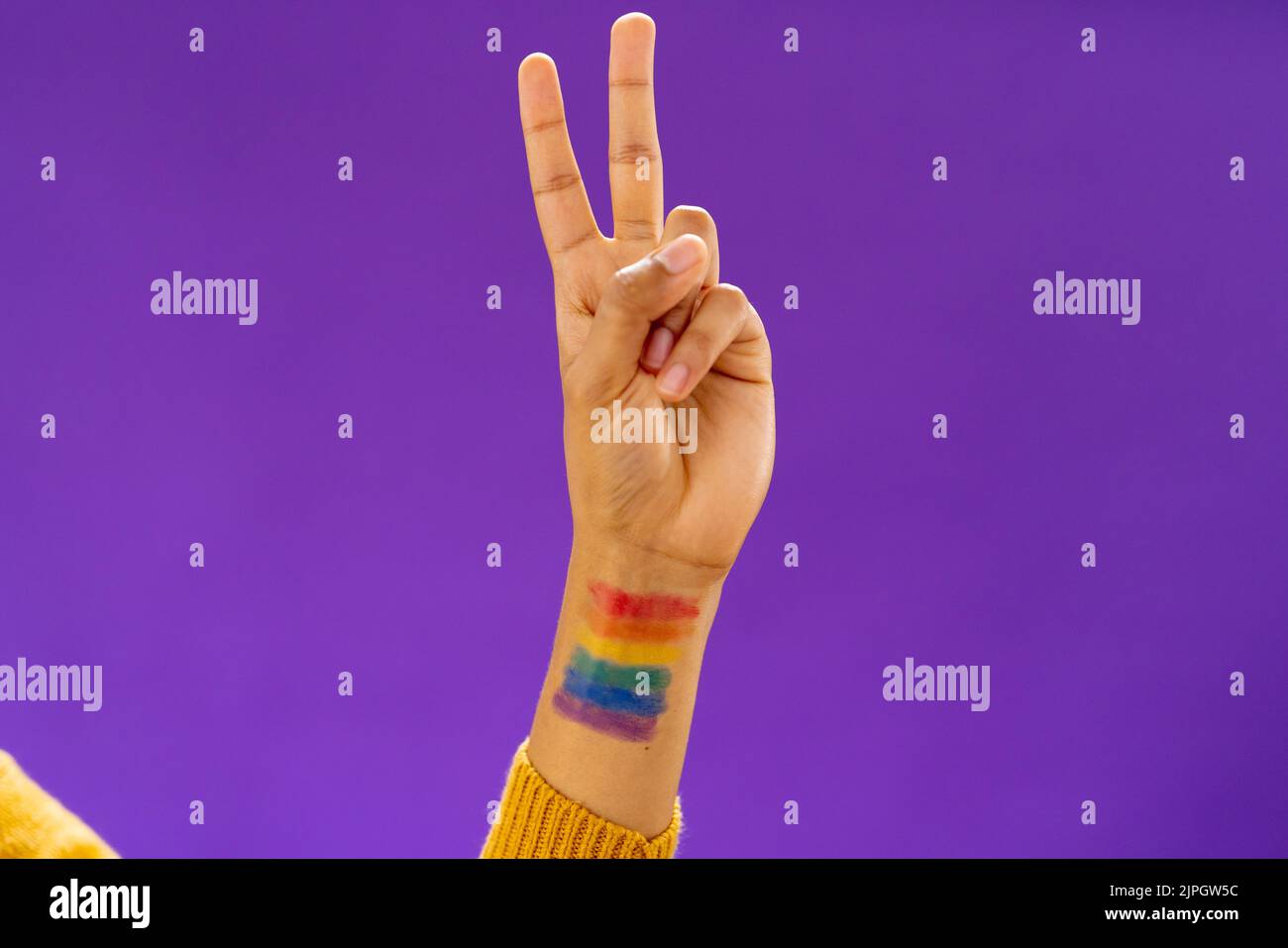Close up of biracial man showing v sign with lgbt flag on arm on purple ...