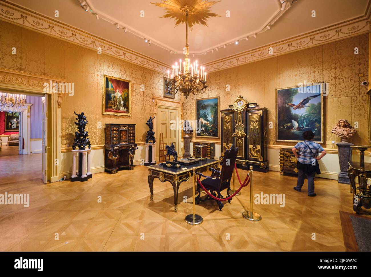 A yellow wallpapered room with desk and hunting paintings. At the ...