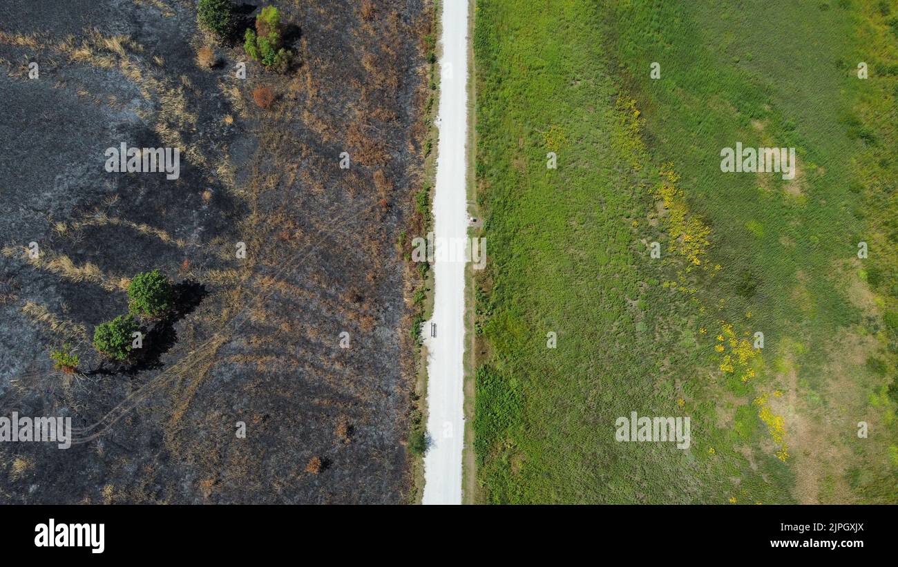 The aerial view of a road between the green meadow and charred land ...