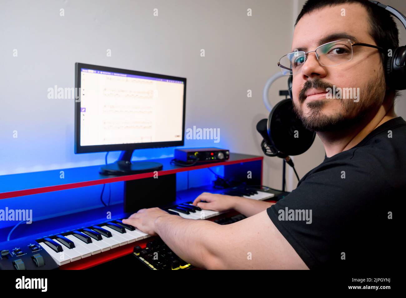 side view of young latin caucasian man with beard, glasses and headphones, sitting playing piano ...