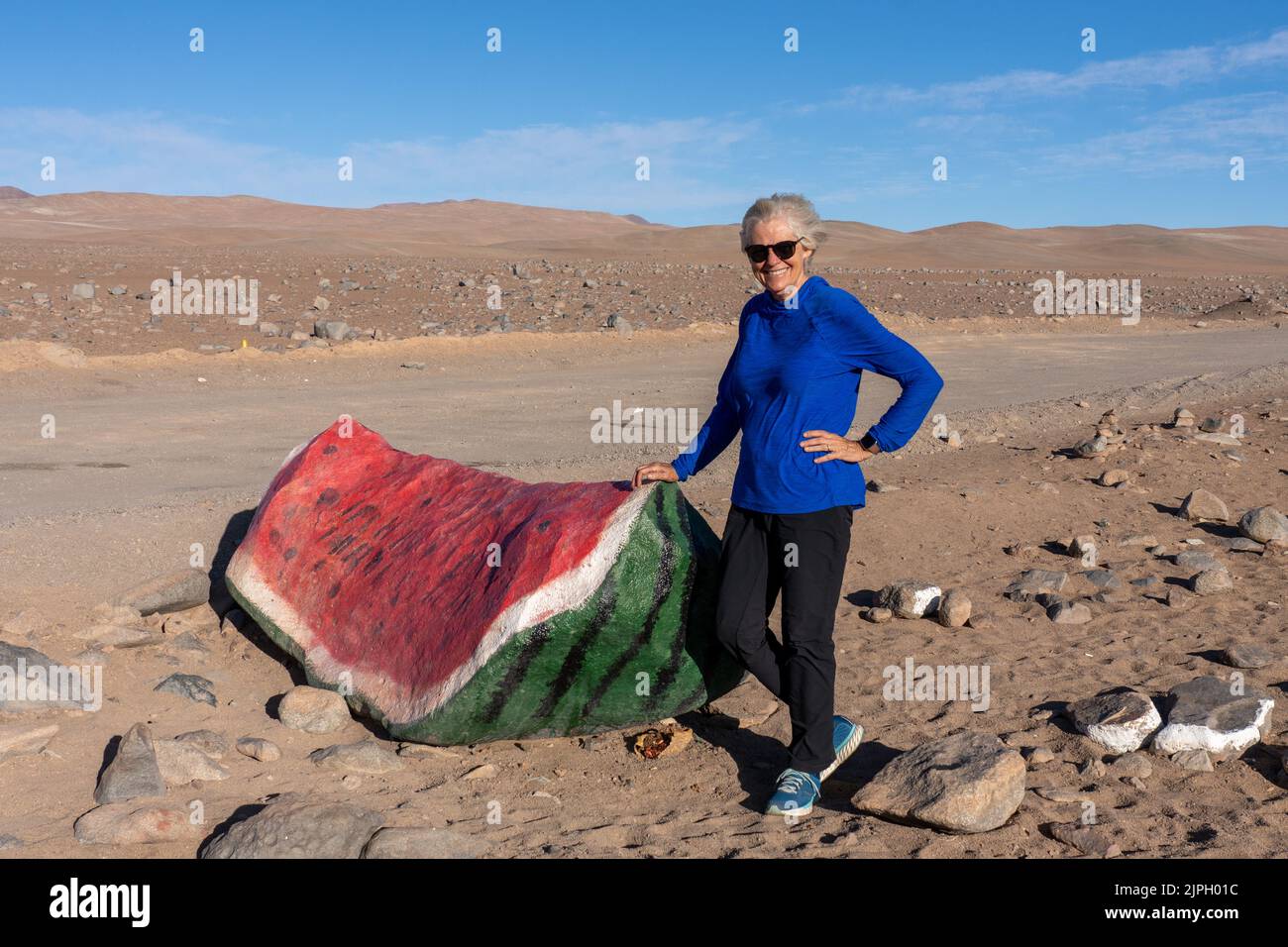 A tourist standing beside a large rock painted as a watermelon ...