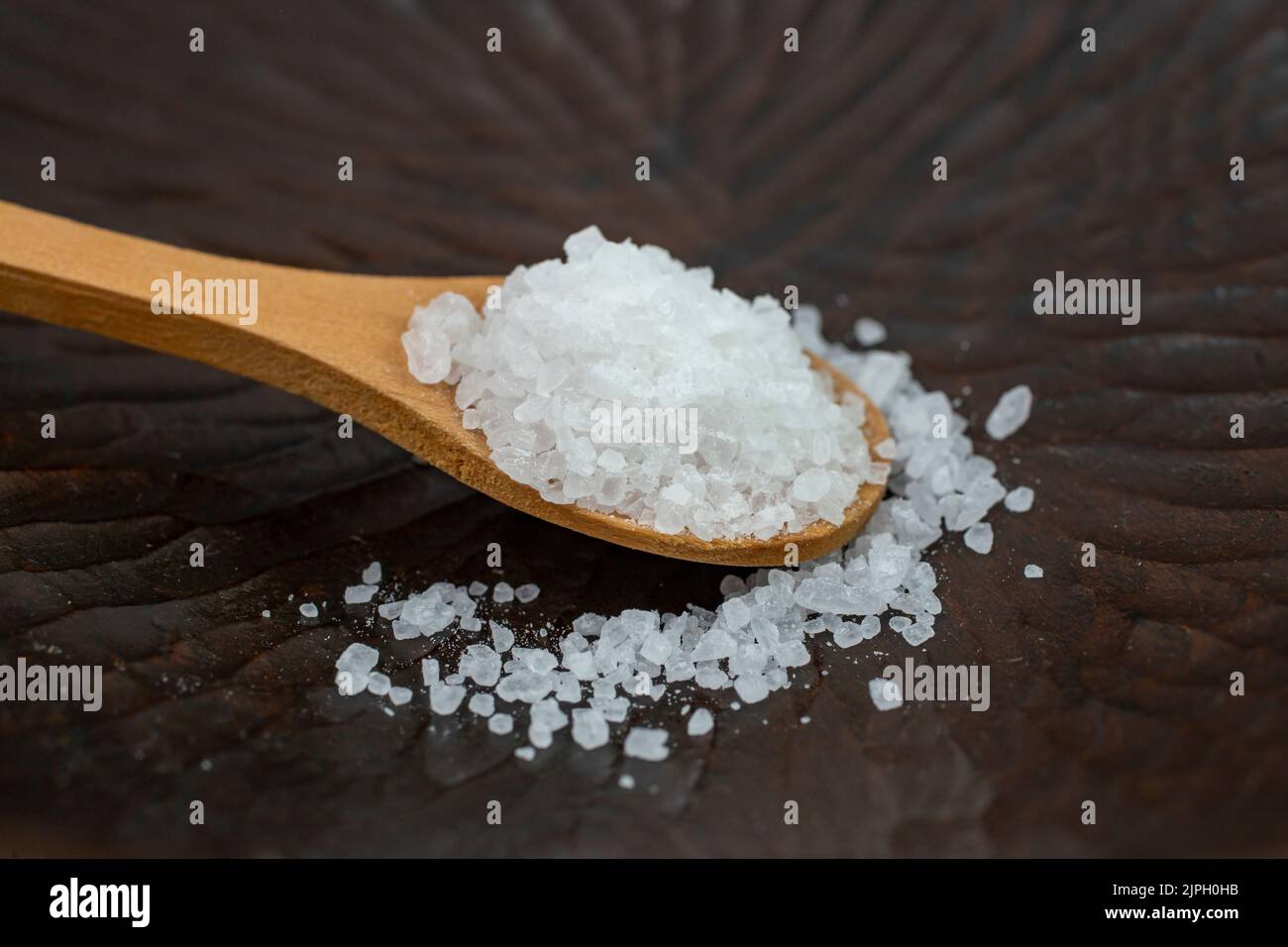 wooden teaspoon full of sea salt in a dark wood bowl, soft focus close ...