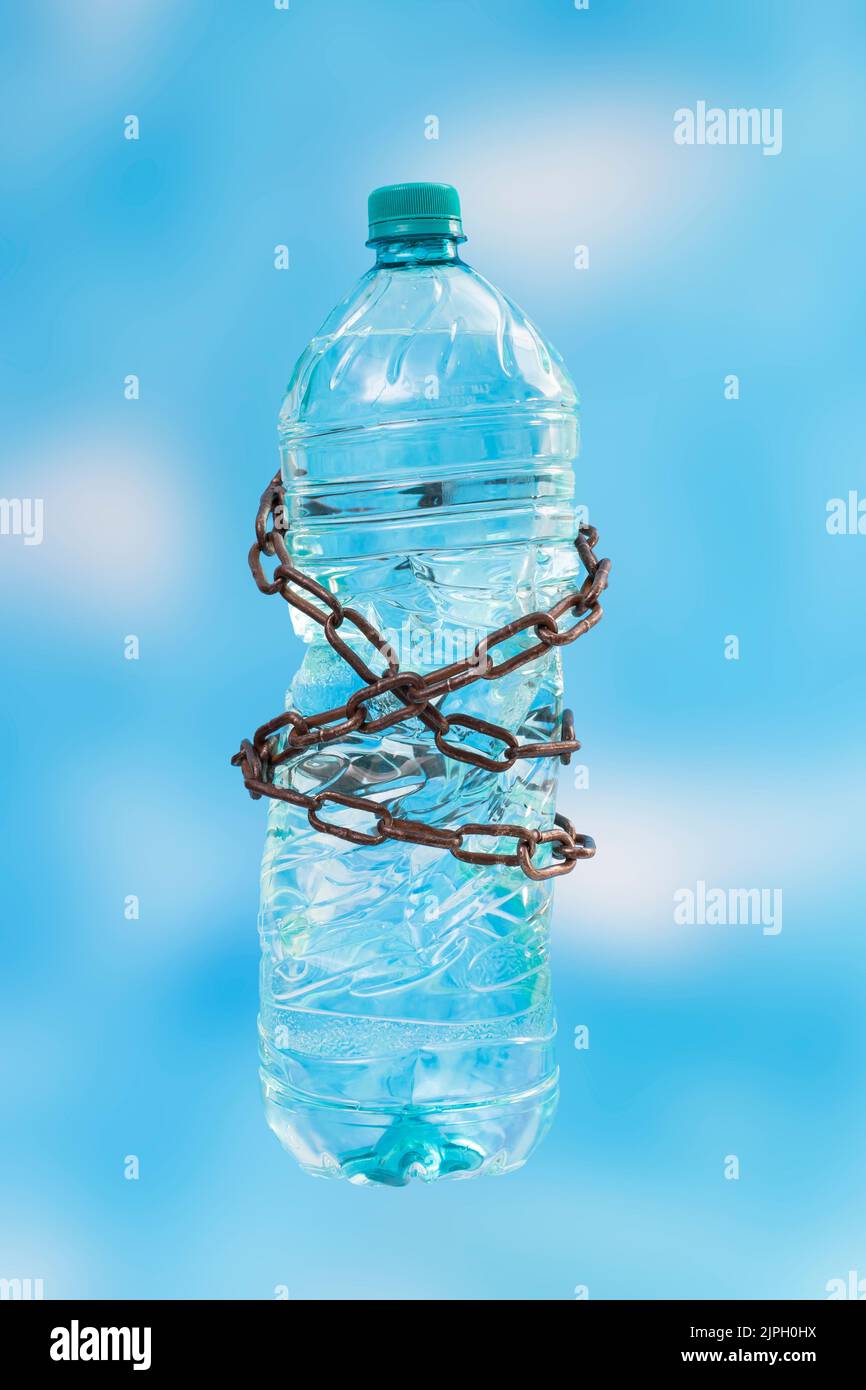 Plastic water bottle tied with rusty chains on blue skyes background ...
