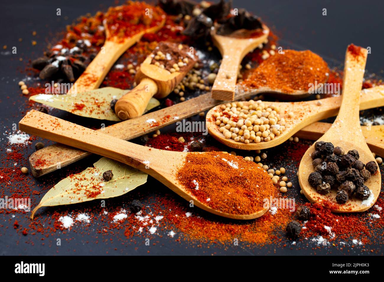 Various spices spilled on black background, with wooden spoons and ...