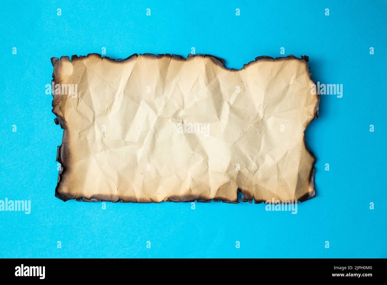 Vintage crumpled paper burned, close up isolated on blue background ...
