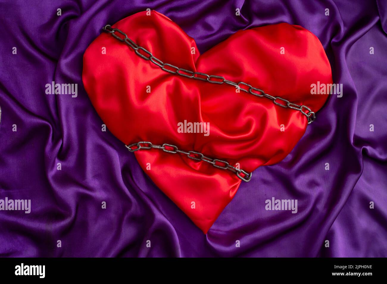 red satin heart tied with chains on purple background, marriage ...