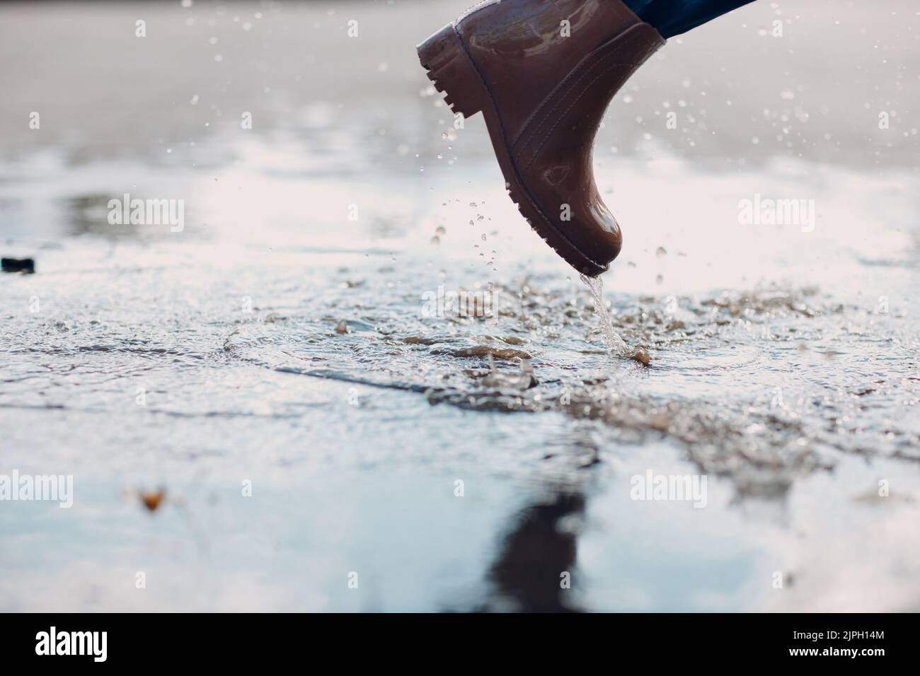 Woman wearing rain rubber boots walking running and jumping into puddle with water splash and ...
