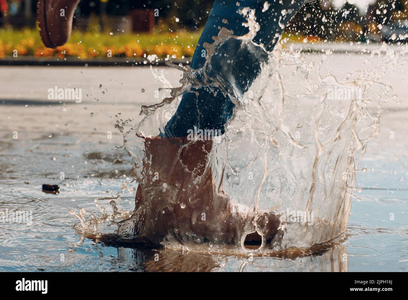 Woman wearing rain rubber boots walking running and jumping into puddle with water splash and ...