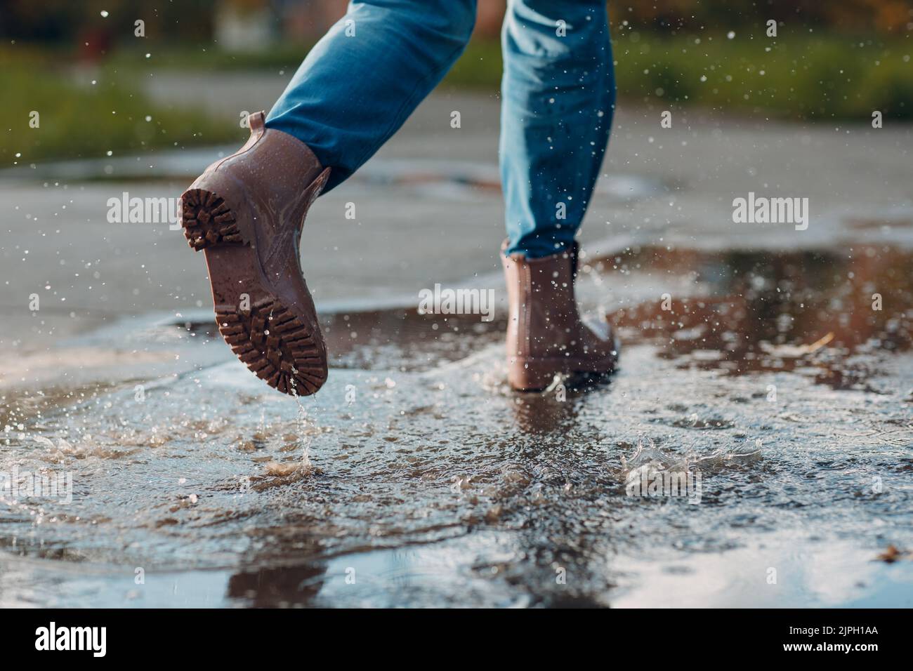 Woman wearing rain rubber boots walking running and jumping into puddle with water splash and ...