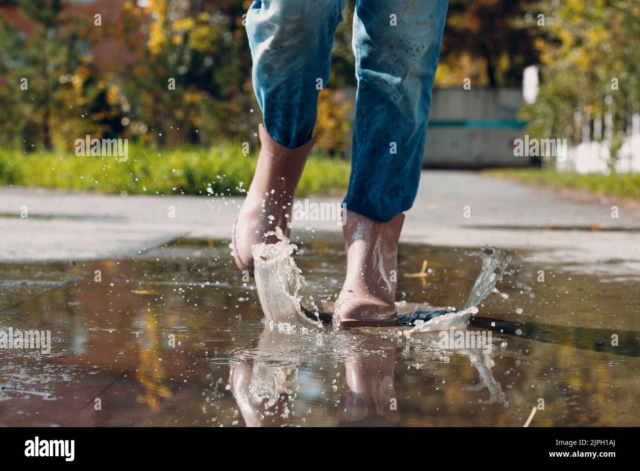 Woman wearing rain rubber boots walking running and jumping into puddle ...