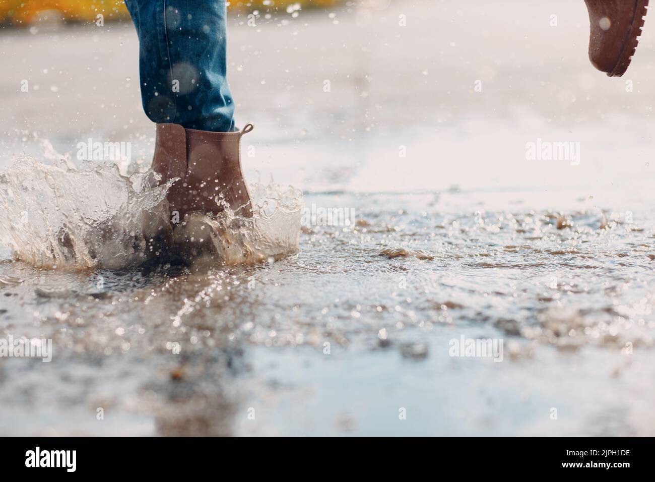 Woman wearing rain rubber boots walking running and jumping into puddle ...