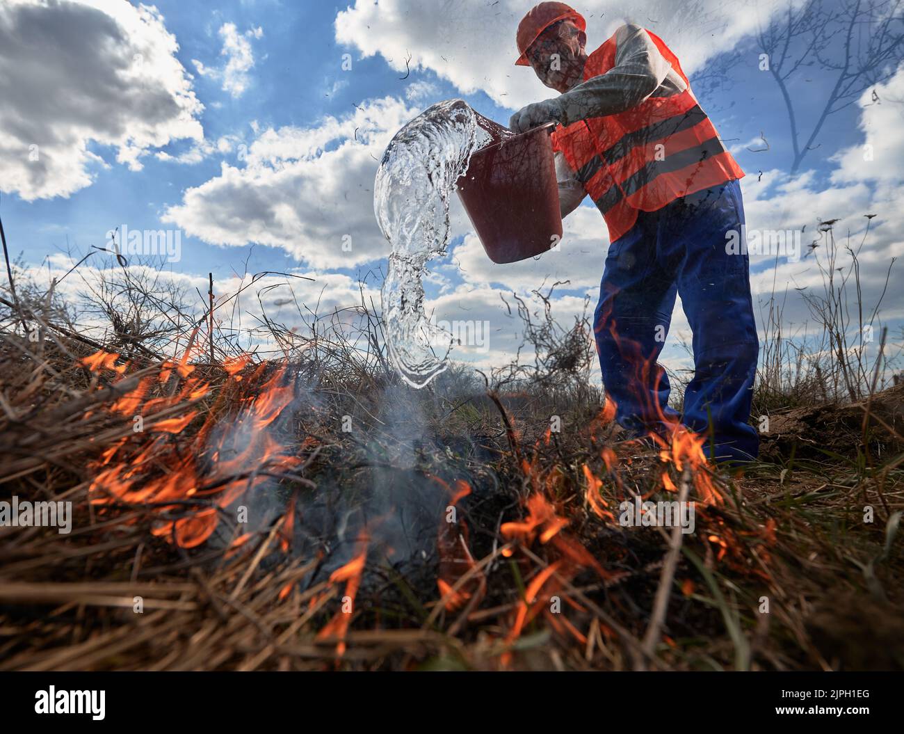 Fireman ecologist fighting fire in field with cloudy sky on background ...
