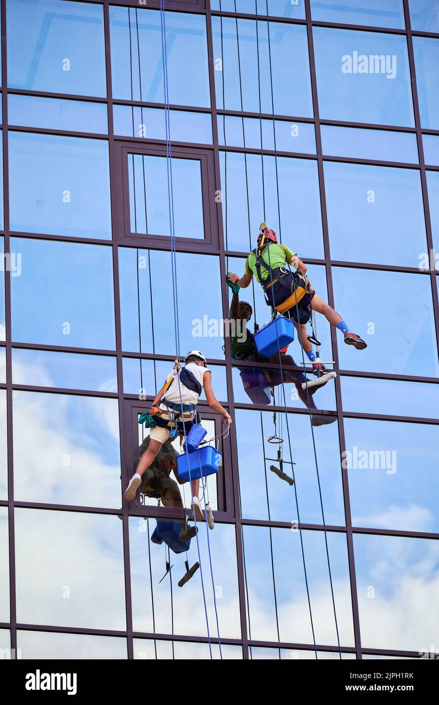 Industrial mountaineering workers washing glass windows of high-rise ...