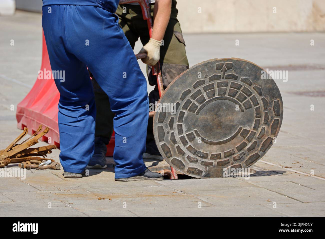 Two workers standing over the open sewer hatch on a street and holding ...