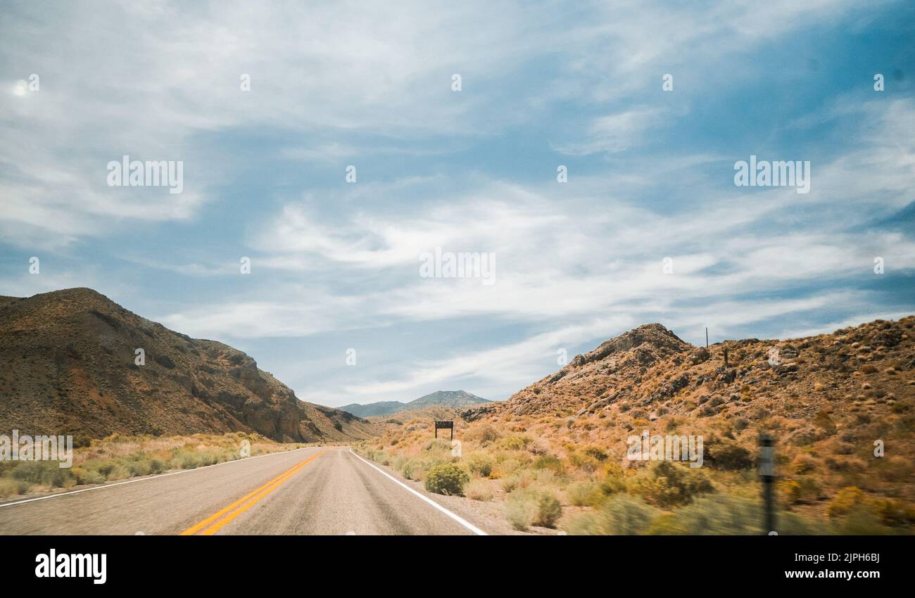 An asphalt road through hills and plants under blue cloudy sky Stock ...