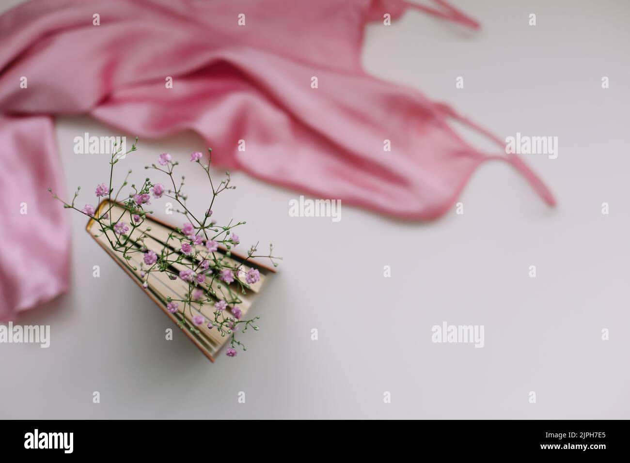 Romantic composition with a book with flowers and pink silk fabric ...