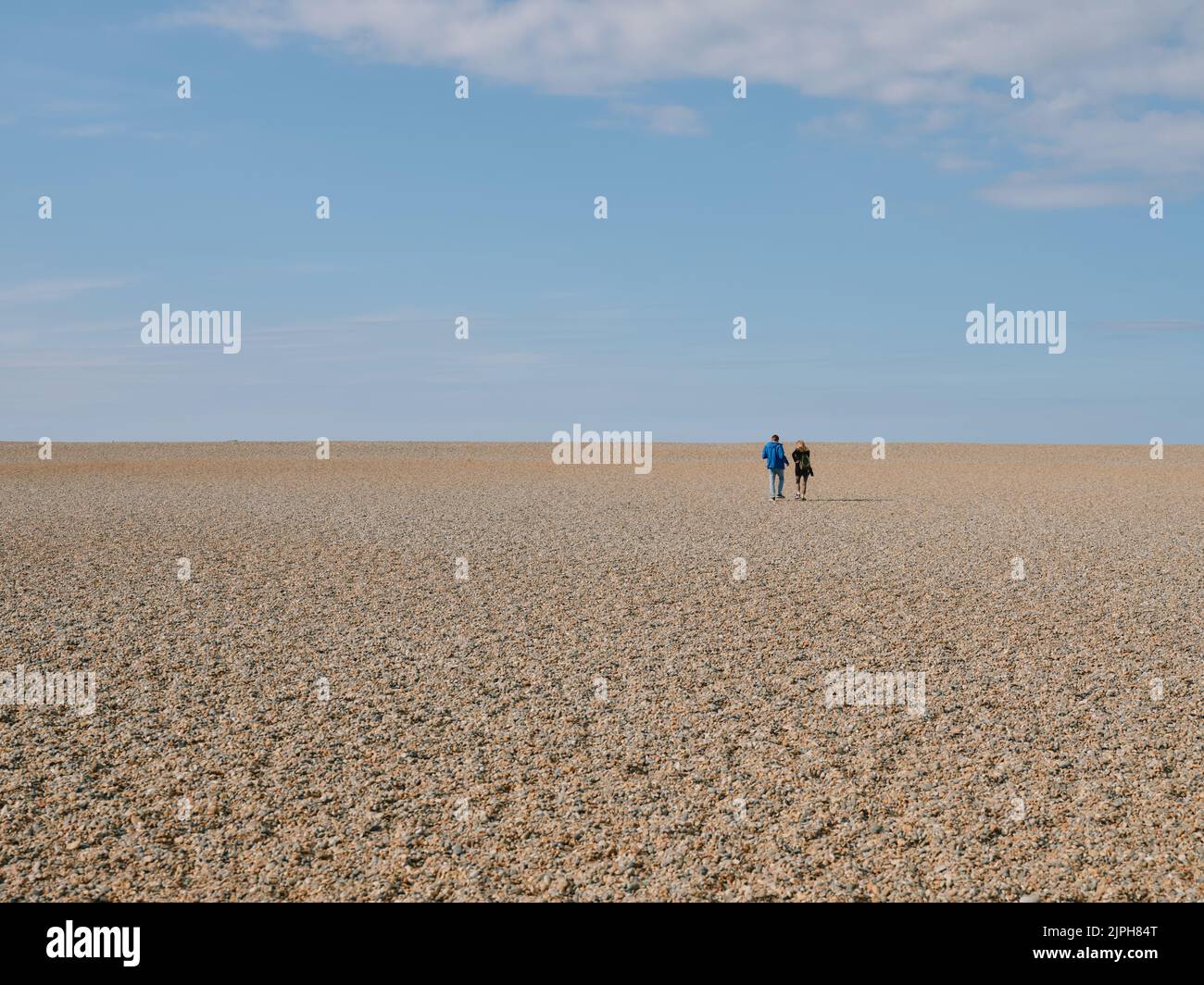 Visiting tourists walking the empty shingle beach summer landscape of ...