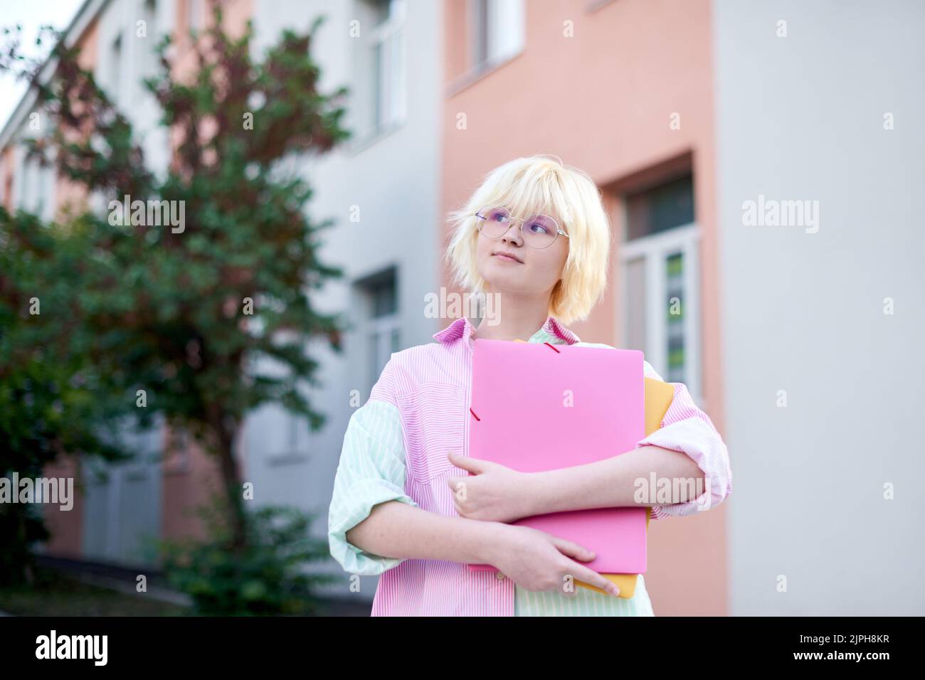 student girl holding pink folder with books walking in school campus ...