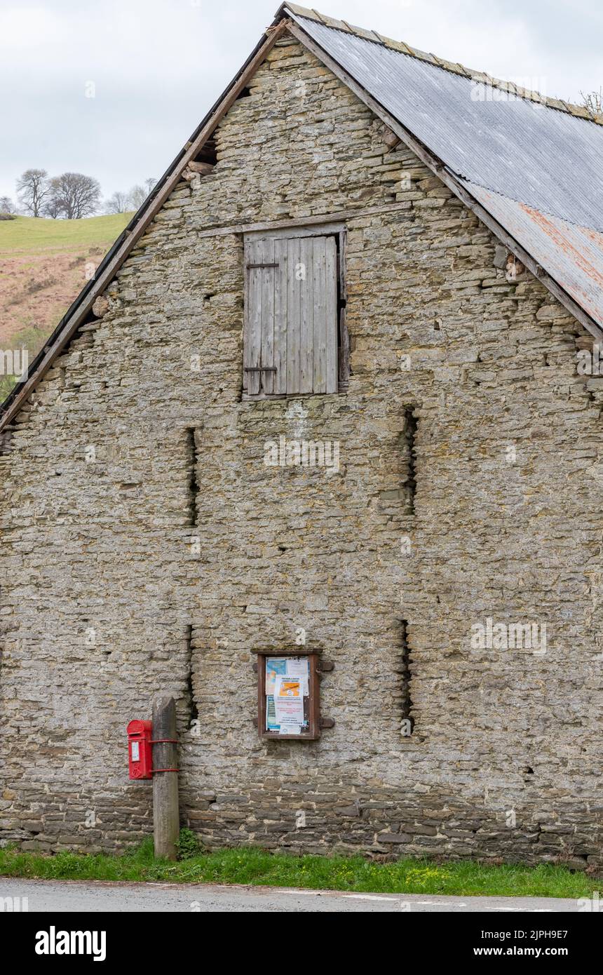 Old stone barn with slit windows, village notice board and royal mail ...