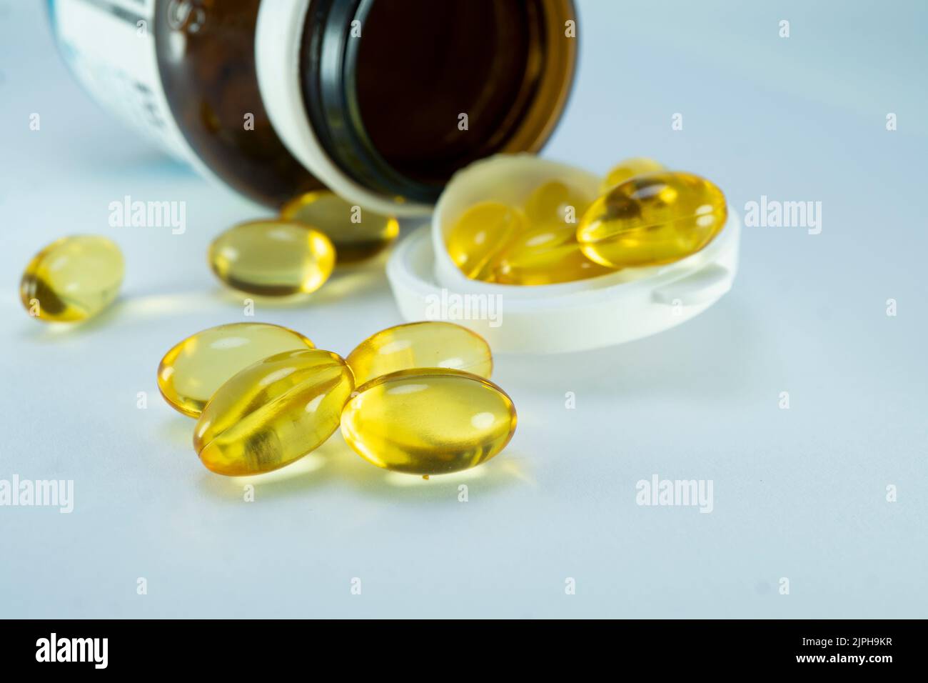 yellow medical pills spilling out of a drug container, isolated on blue ...