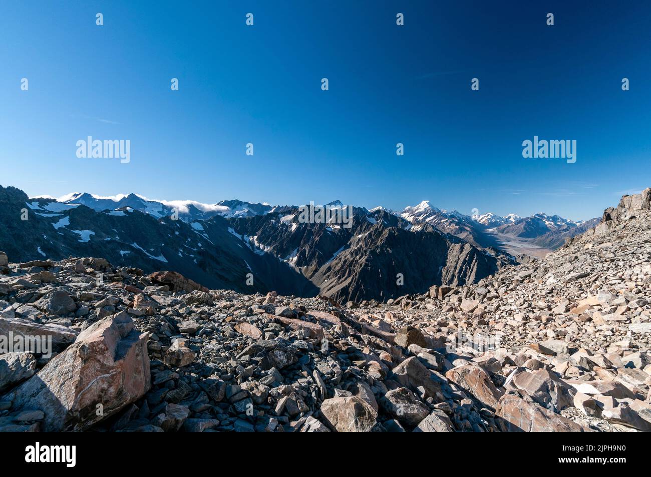 On a rock-strawn summit towards the snow-capped Aoraki / Mount Cook on ...