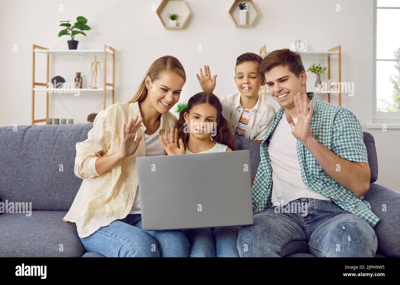 Happy family sitting on the couch, making a video call and waving hello ...