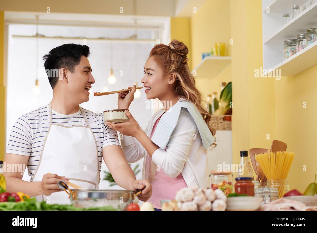 Young woman feeding her boyfriend when he is cooking dinner Stock Photo ...