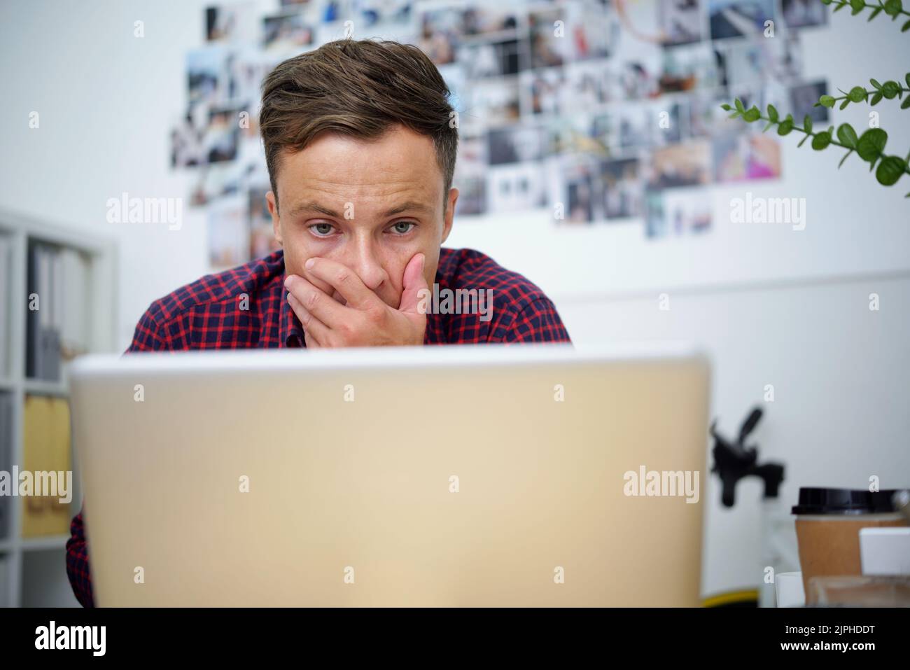 Shocked man covering his mouth when reading e-mail on laptop screen ...