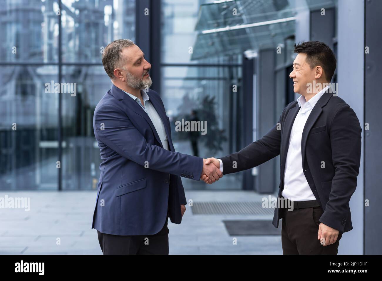 Two businessmen, bosses greet each other by shaking hands, a diverse group of men in business ...