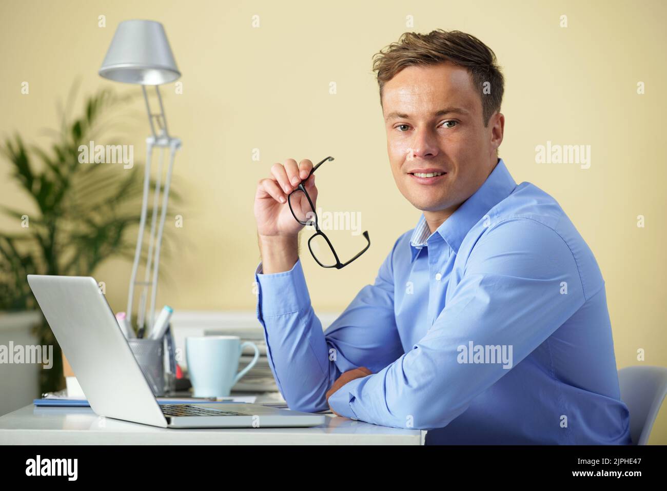 Portrait of handsome office worker with glasses in his hand smiling at ...