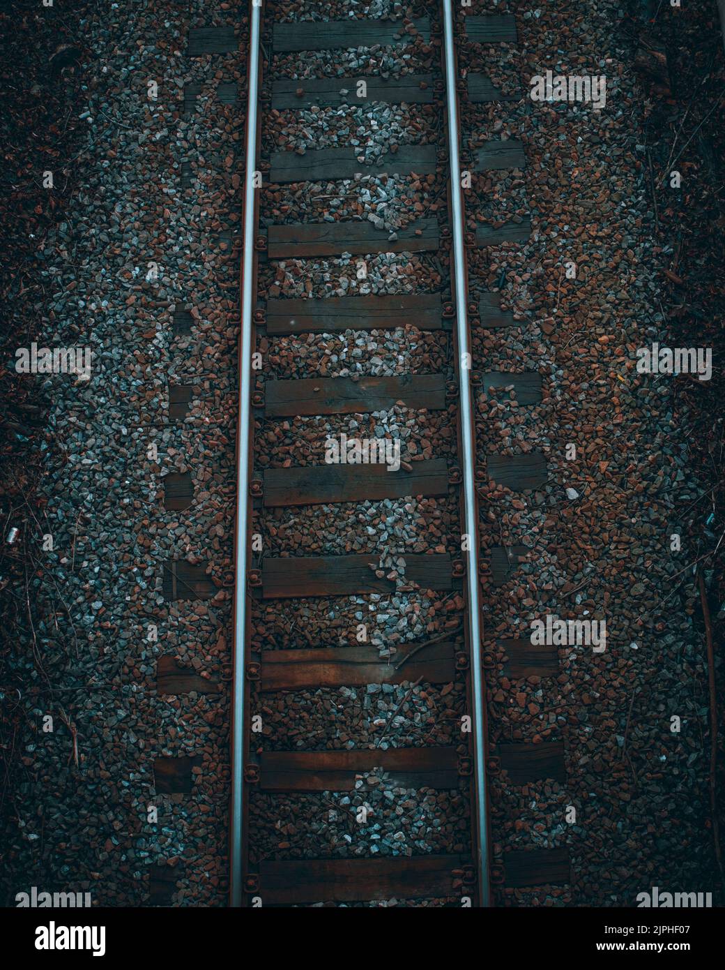 A vertical shot of an old rusty railroad surrounded by grey pebbles ...