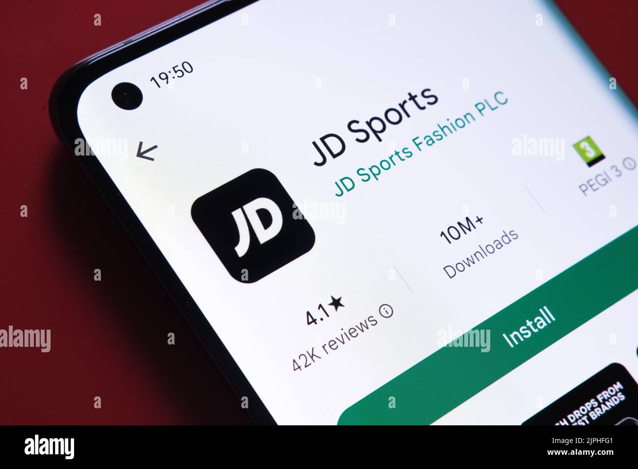 JD Sports app seen in Google Play Store on the smartphone screen placed on red background. Close ...