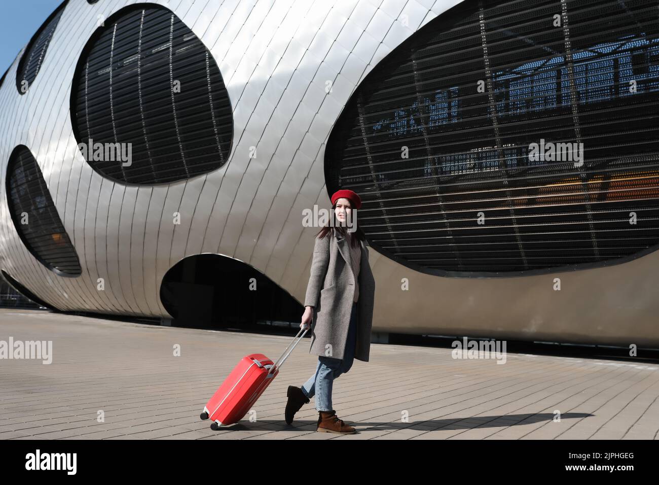 young woman tourist with a red travel suitcase by the futuristic facade ...