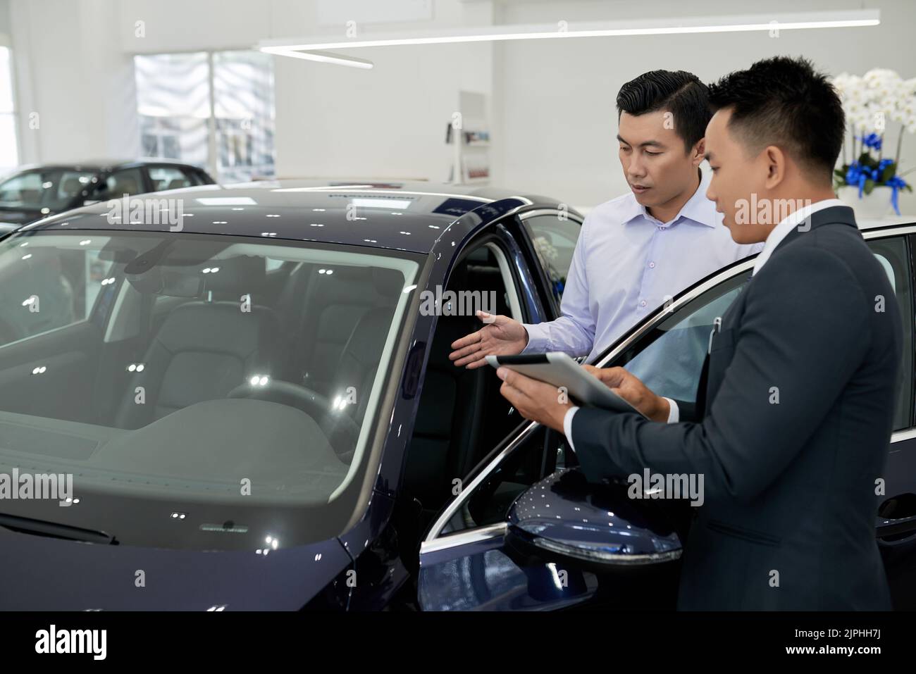 Young Asian salesman showing new car to customer Stock Photo - Alamy