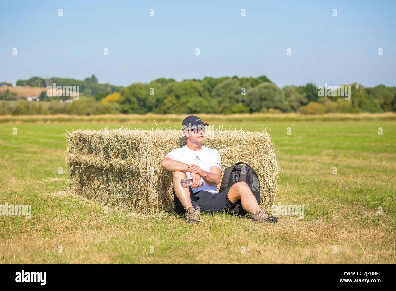 Front view of a man sat in front of a straw bale in shorts and cap with ...
