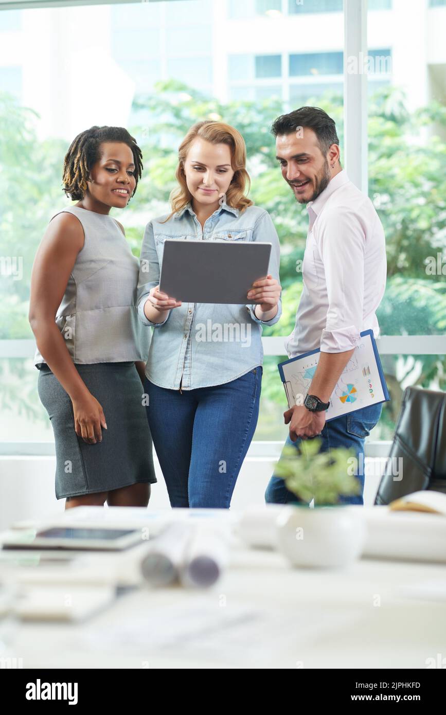 Multi-ethnic group of colleagues standing at spacious open plan office ...