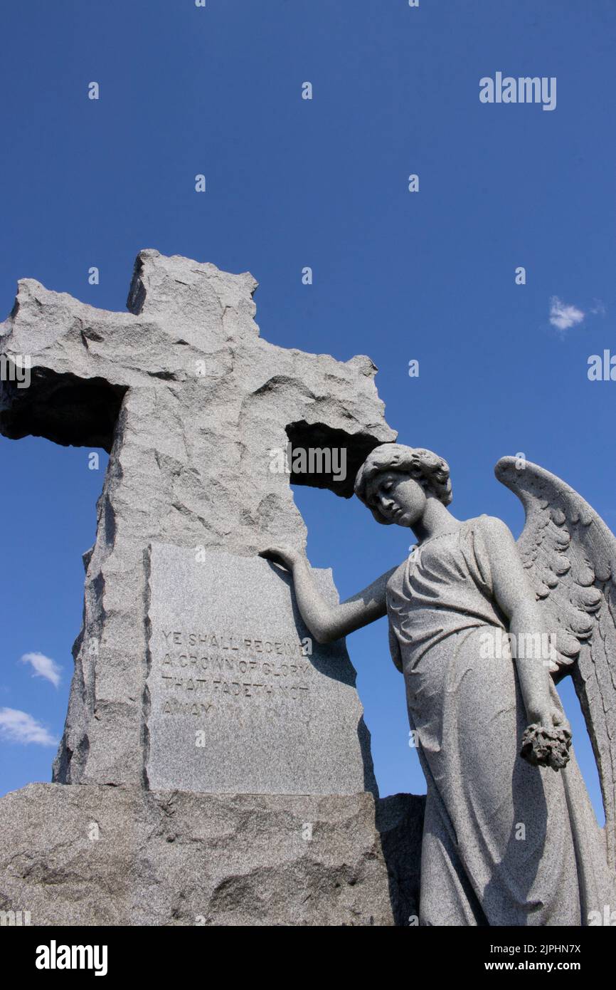 A stone angel stands with her hand on the cross and her wings partially spread with a look of ...