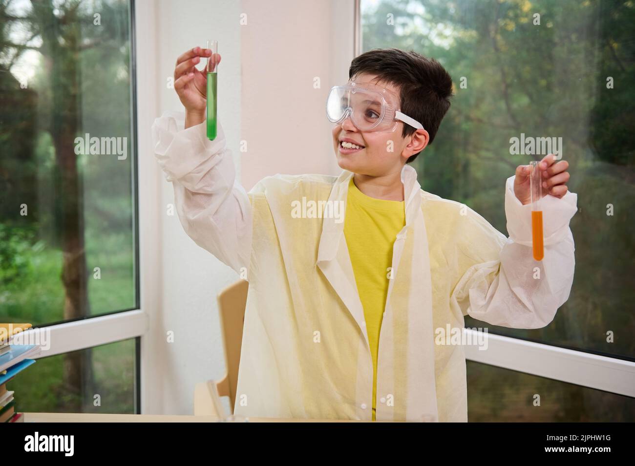 Smart pupil, teenage schoolboy in protective goggles and white lab coat ...