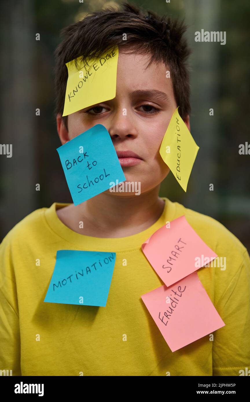 Bored, tired, sad schoolboy with glued colored paper for notes on his ...