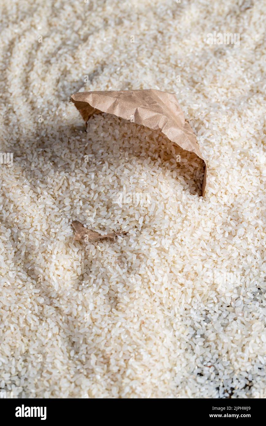 a pile of white rice in a paper bag and on the table, white uncooked ...