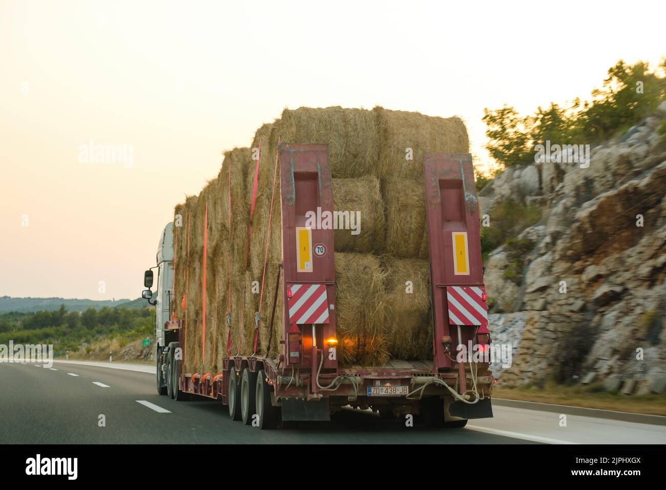 Truck drives on highway transporting bales of hay and straw at back ...