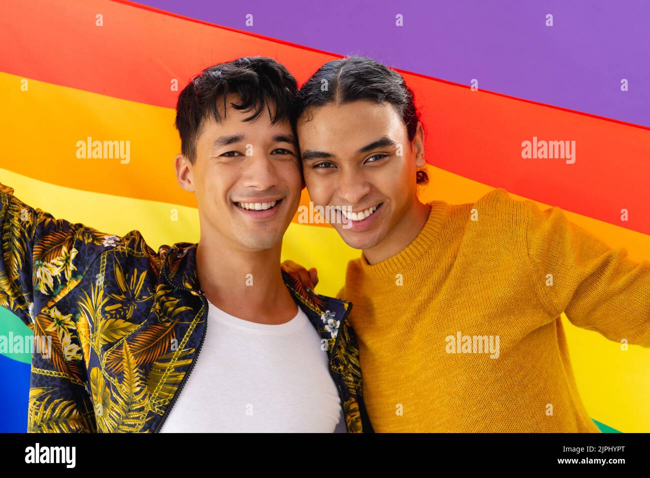 Portrait of happy biracial male couple embracing and holding lgbt flag ...