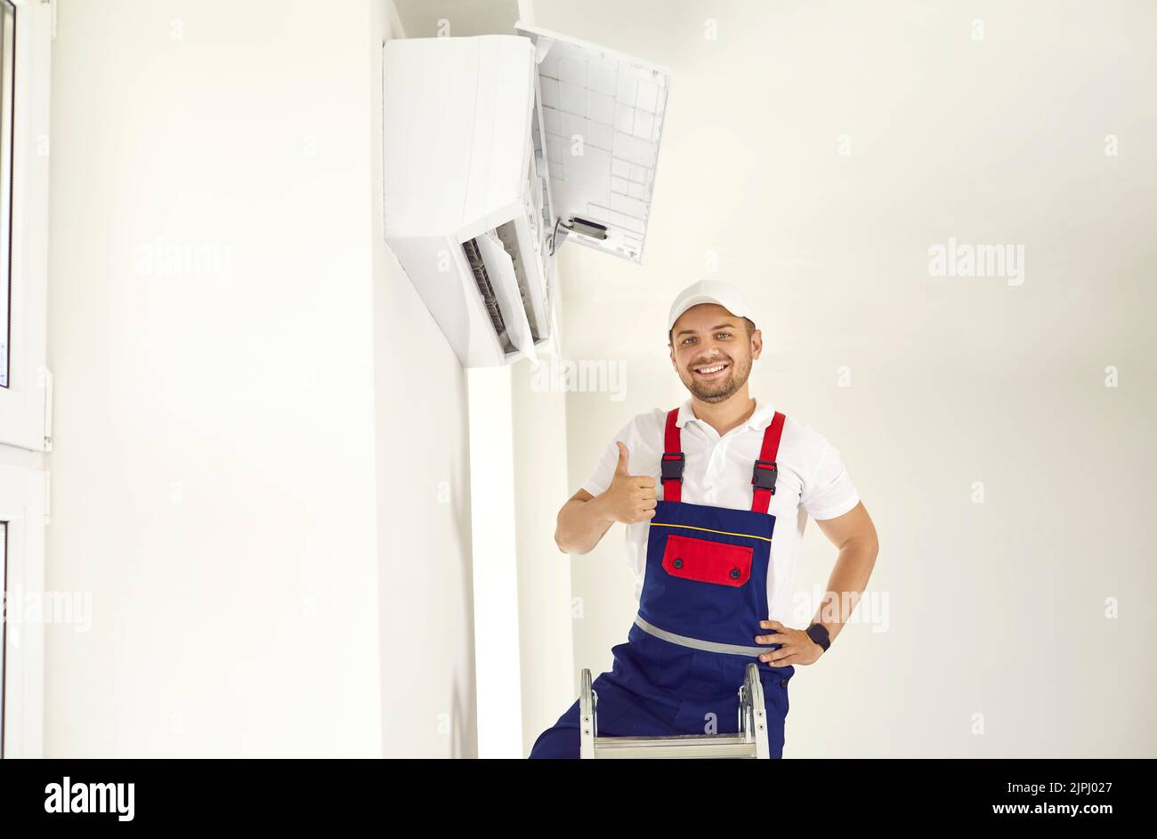 Male worker showing thumbs up after repairing or installing wall air ...